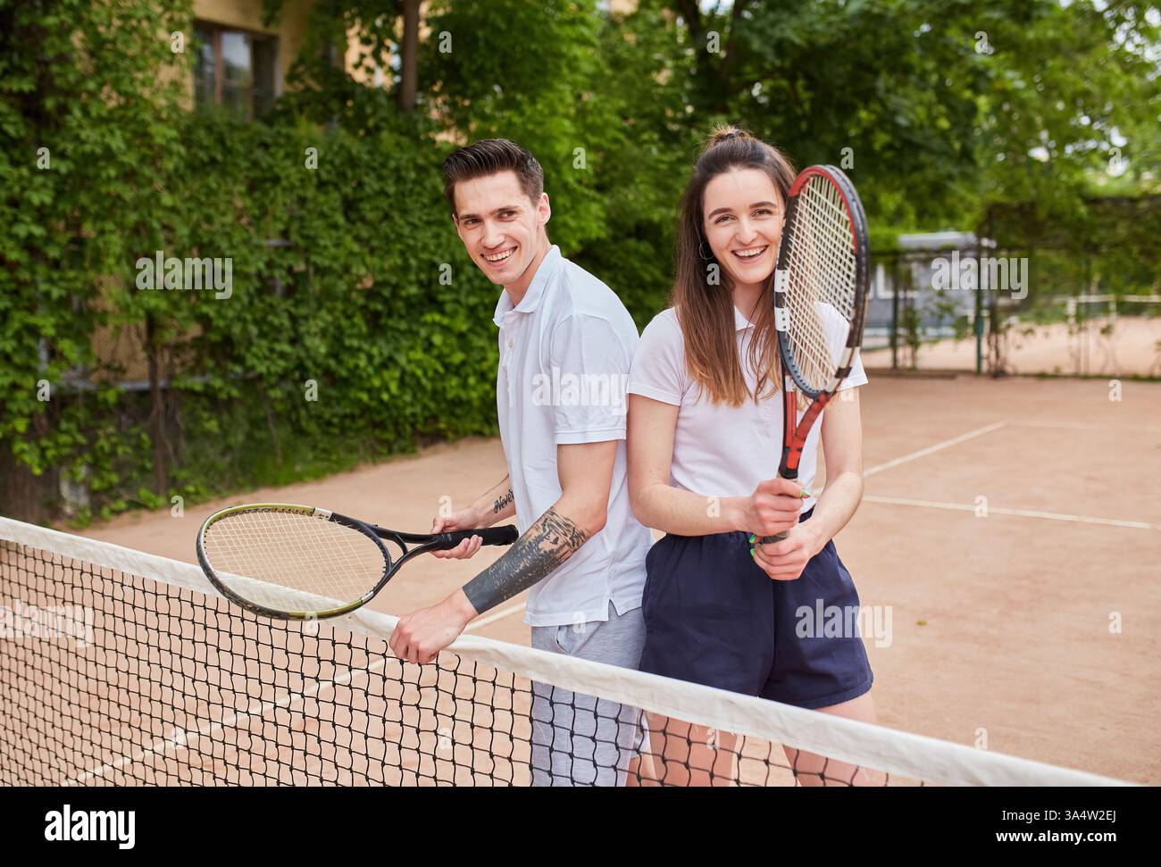 A man and woman stand back-to-back on a tennis court, both holding ...