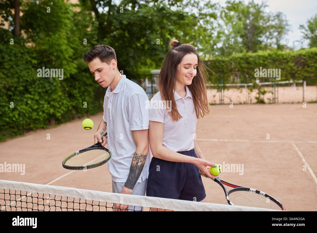 A man and woman stand back-to-back on a tennis court, both holding ...
