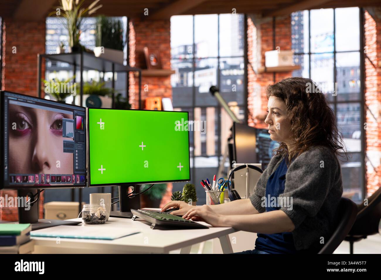 Female graphic designer uses editing software and green screen for photo retouching in a well ...