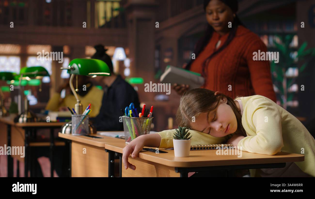 Teacher waking up her student sleeping on the study desk at the library ...