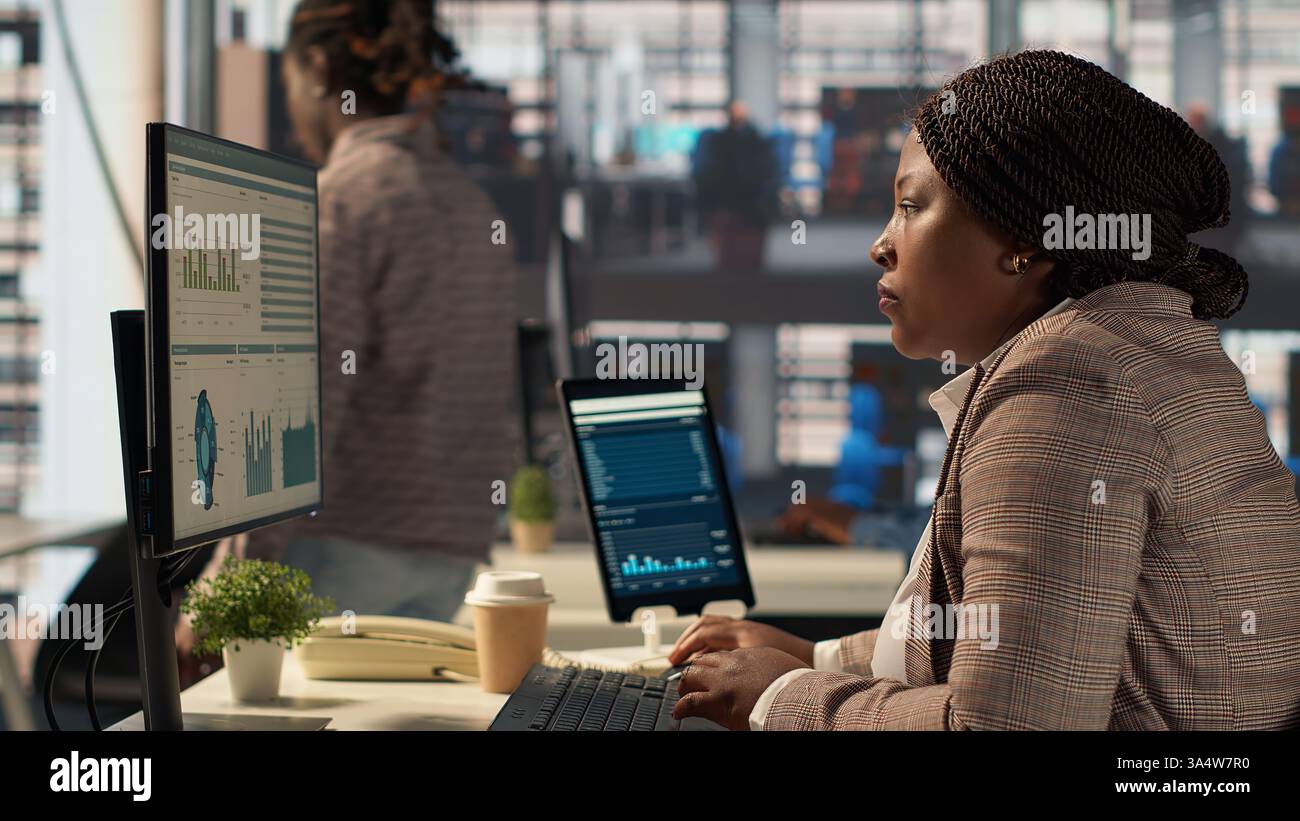 Confident businesswoman at her office desk working on report writing and answering emails ...