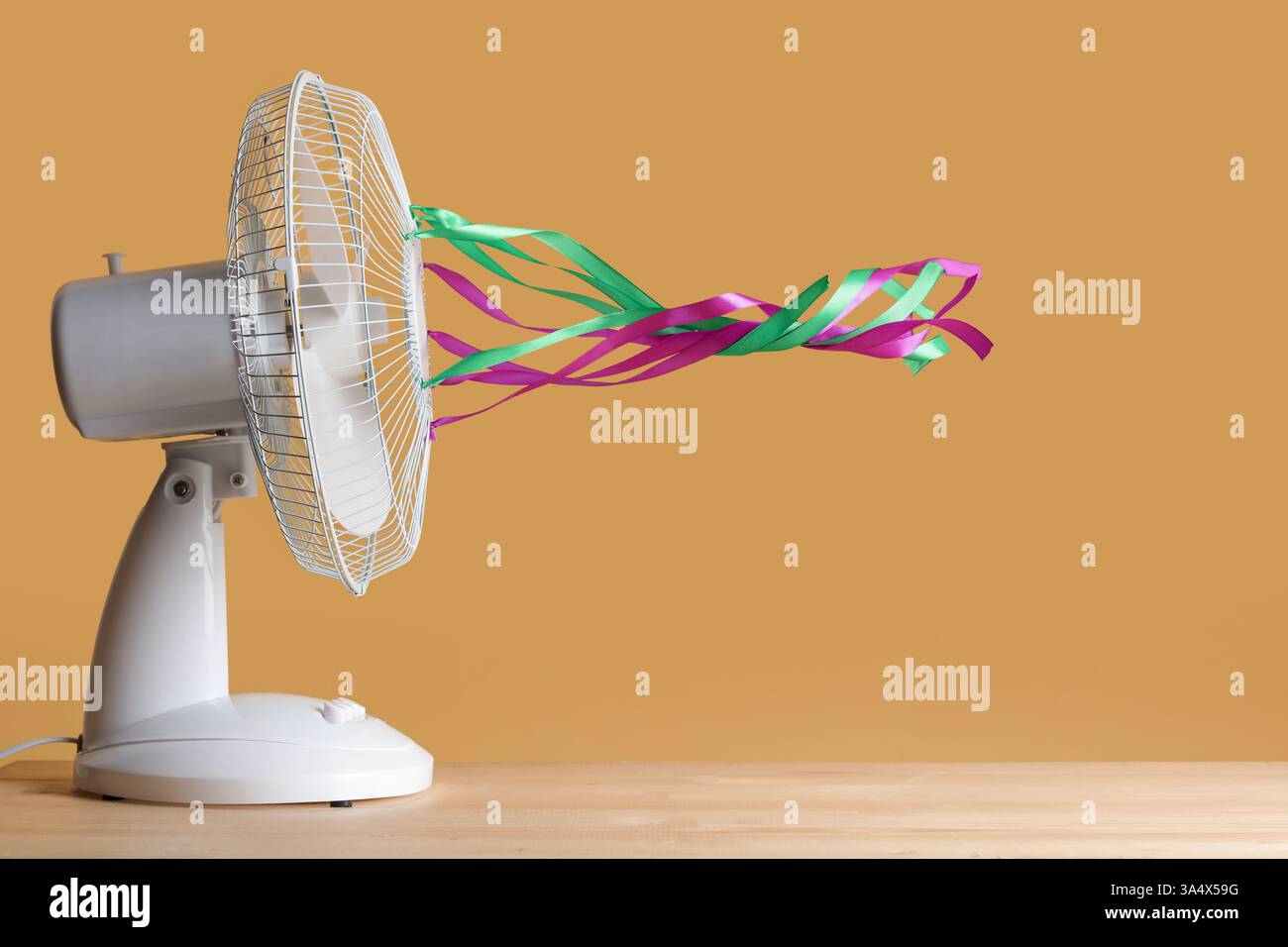 Electric fan with fluttering ribbons on table against yellow background ...