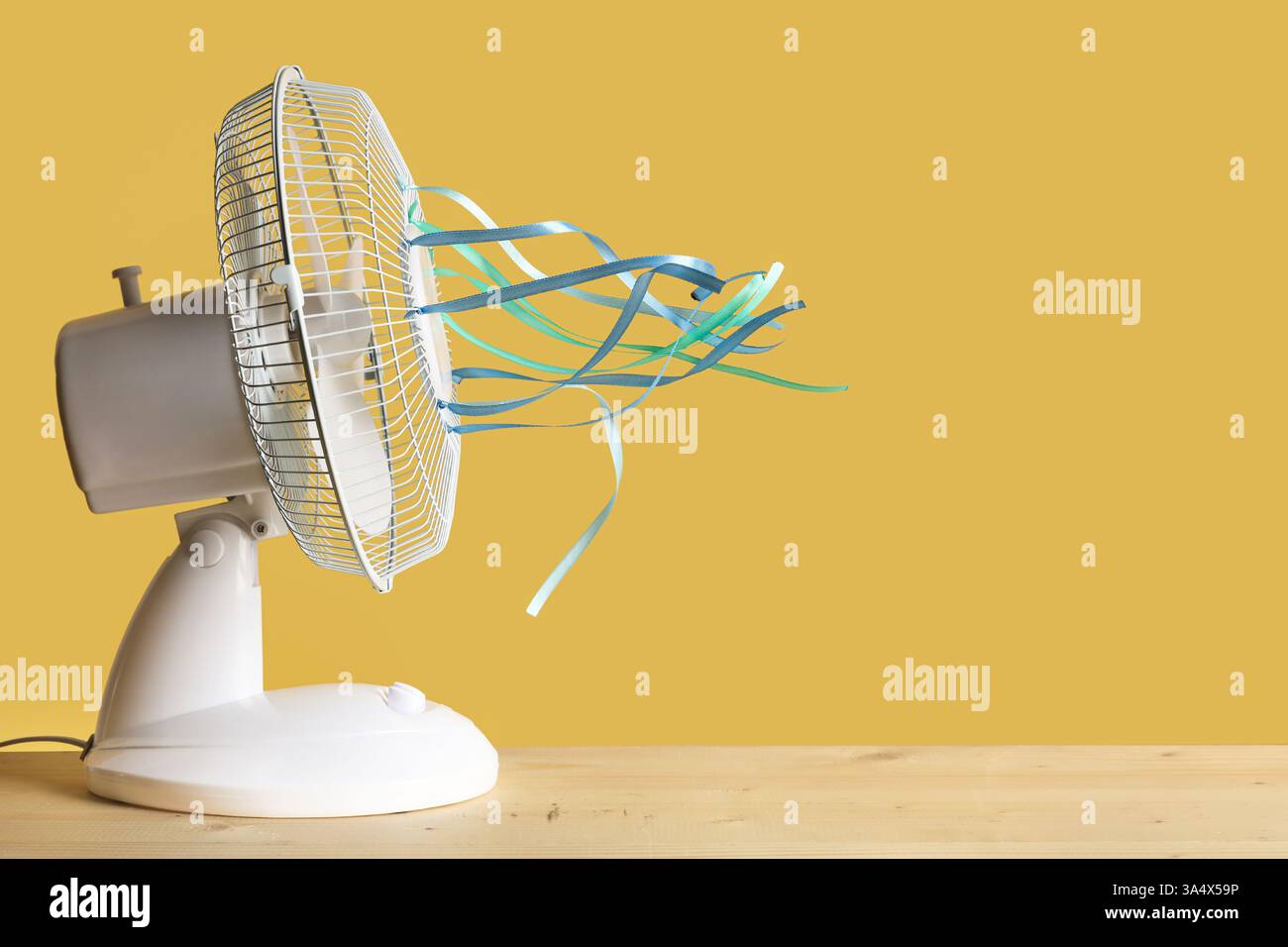 Electric fan with fluttering ribbons on table against yellow background ...