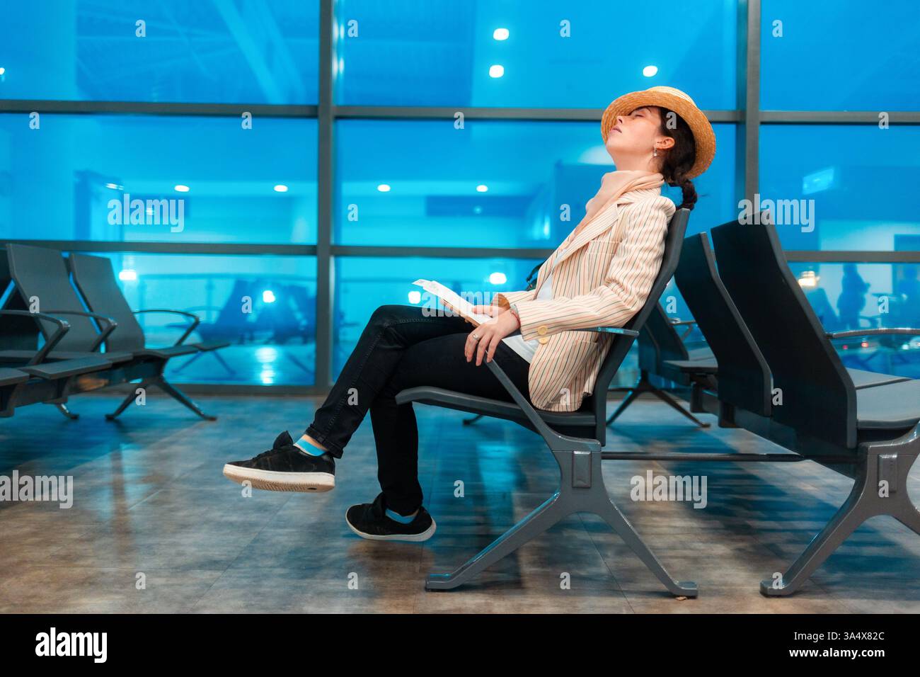 Side view of young Caucasian elegant sleeping woman holds boarding pass and sitting on chair at ...