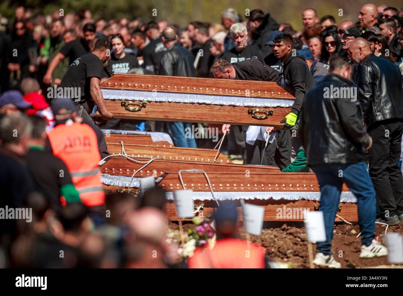 Coffins are placed next to the graves as people gather at a cemetery ...