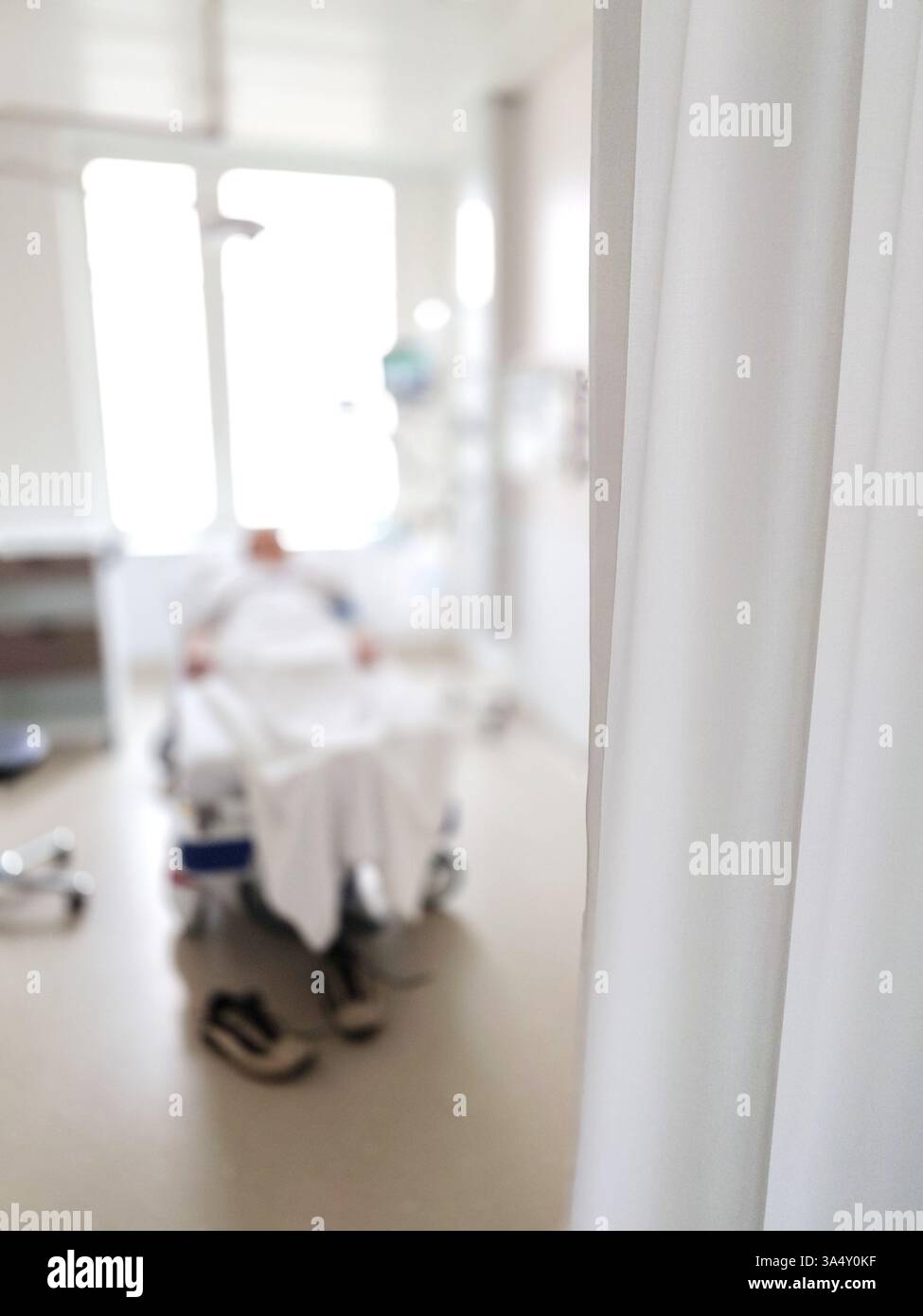 Blurred, unrecognizable patient on a hospital bed inside recovery room. Natural window light ...