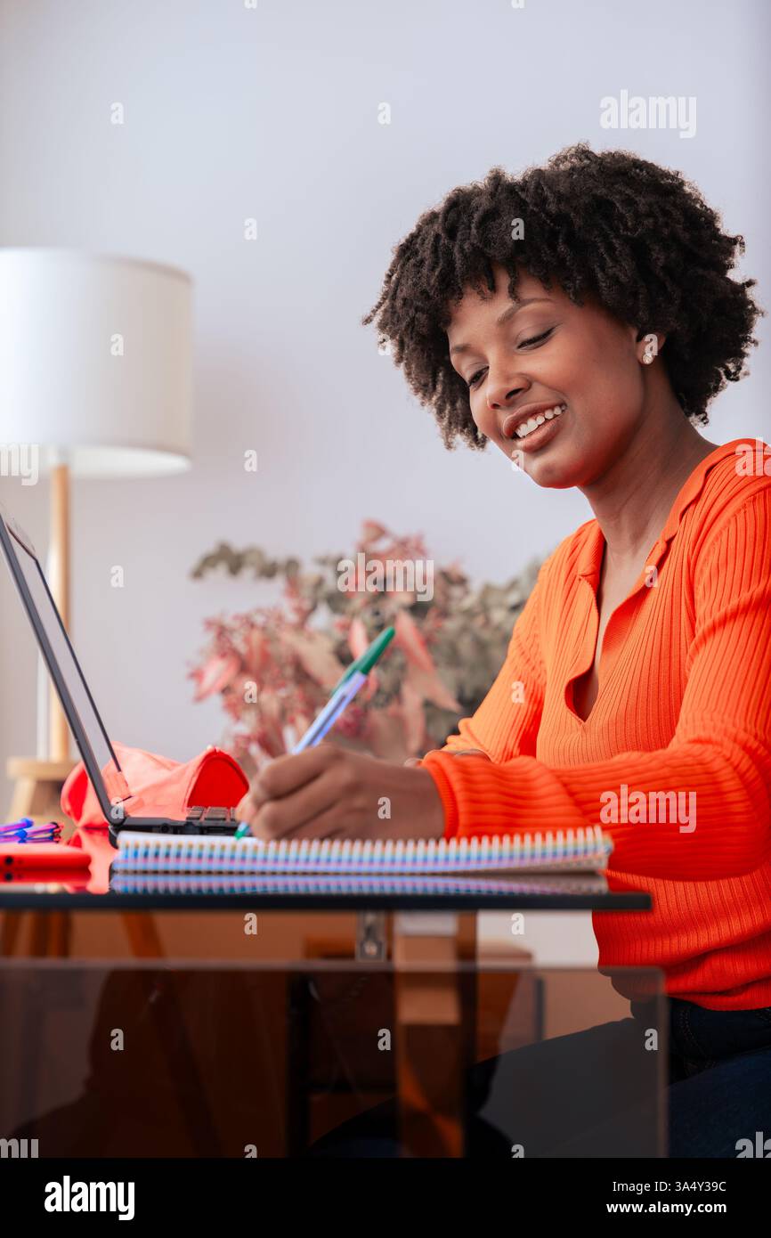 African American student studying at home, writing in notebook, using ...