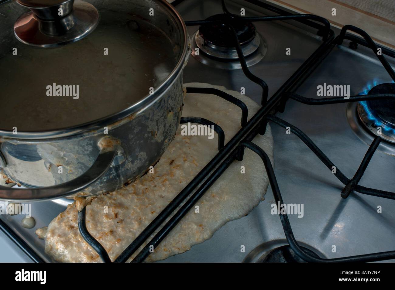 Oatmeal spilled from under the lid of the pot onto the gas stove while ...