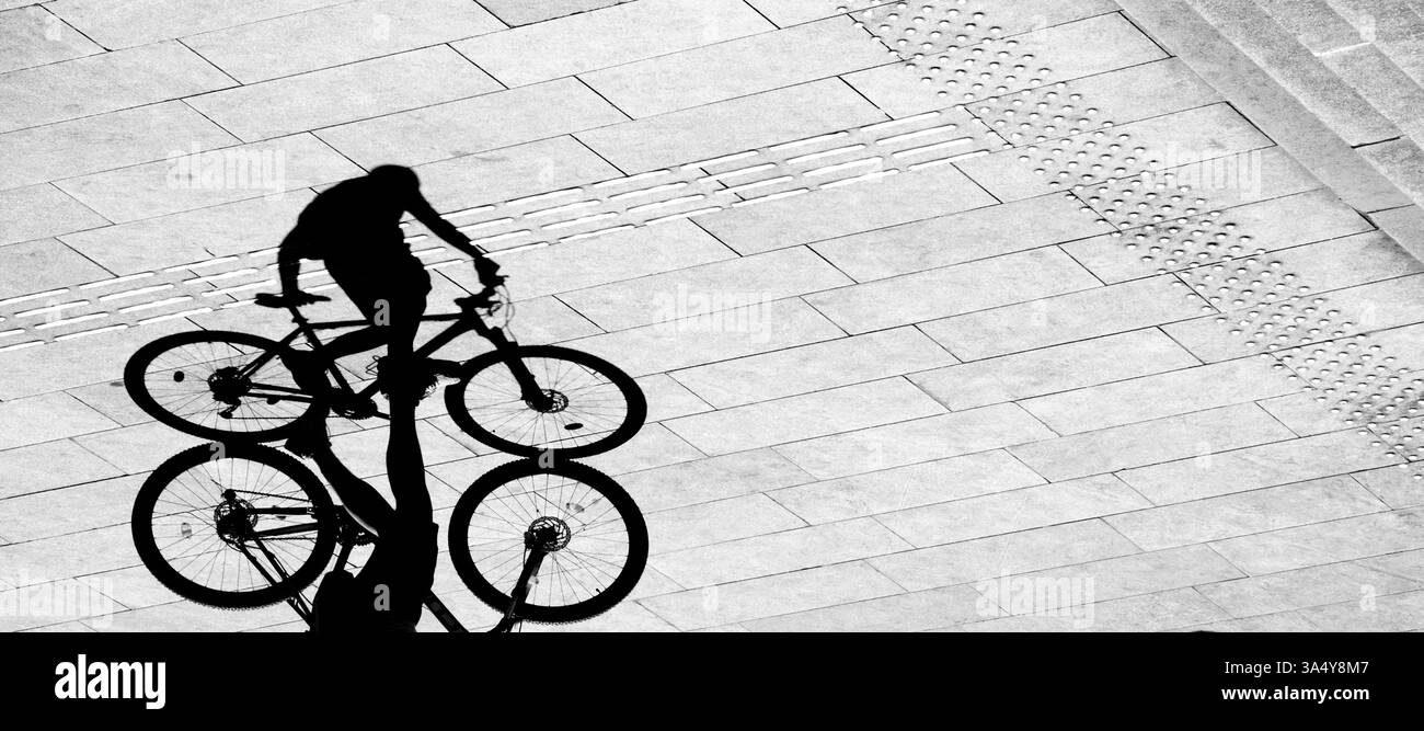 Shadow silhouette of a cyclist pushing a bike on town tiled square with ...