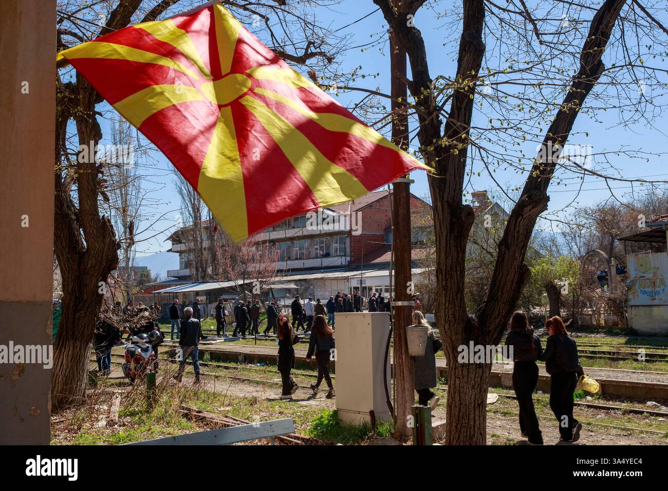 A Macedonian flag is lowered at half mast as people walk along railway ...