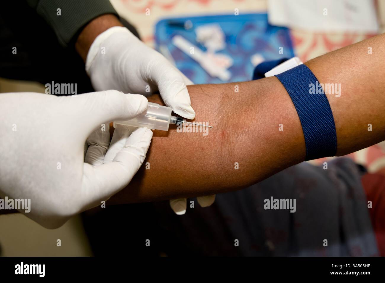 A healthcare worker collects a blood sample from a patient's arm in a ...