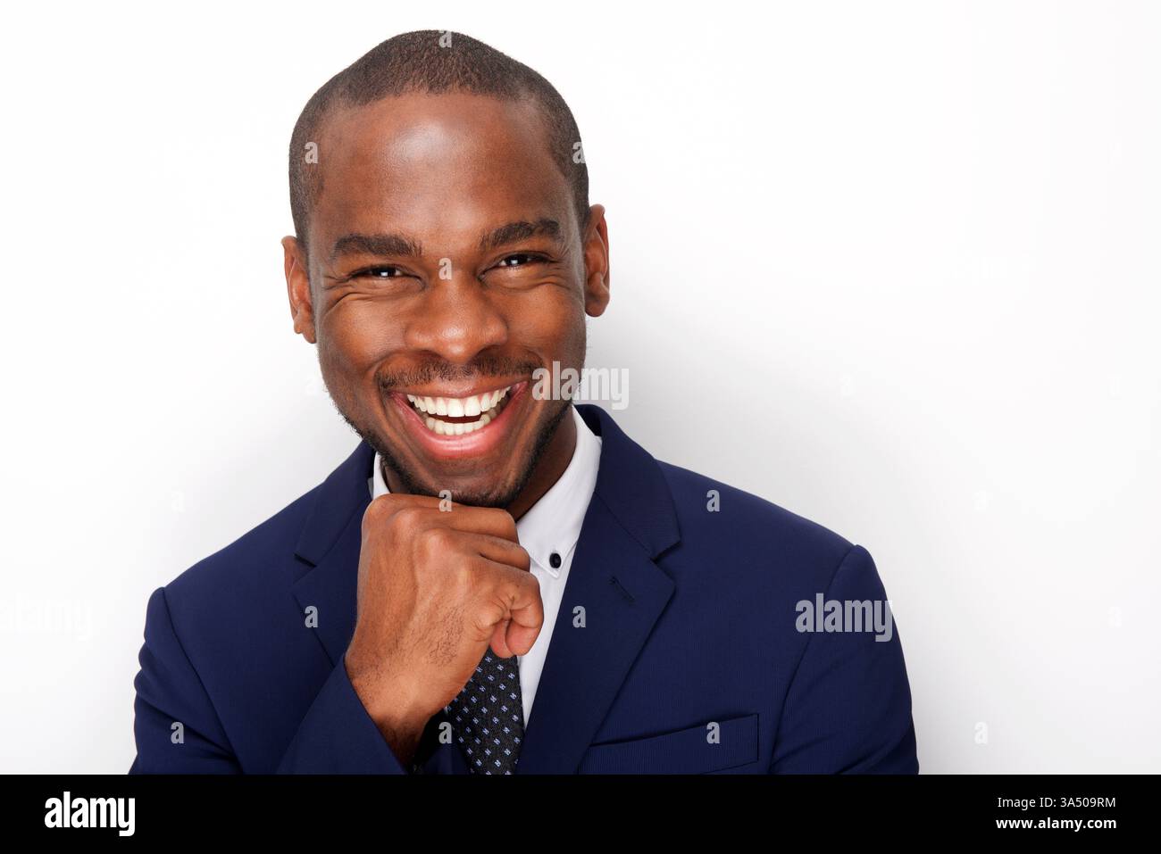 Smiling Black businessman leaning chin on fist standing against white ...
