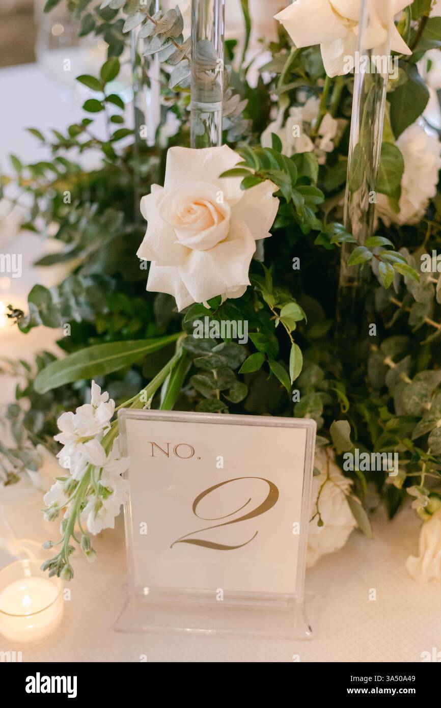 A stunning centerpiece featuring white roses and greenery marks table ...
