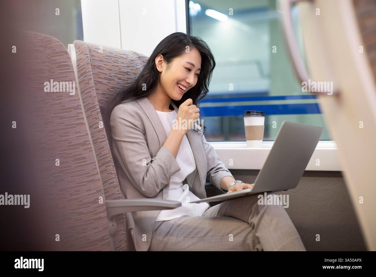 Smiling Chinese business woman using laptop sitting with crossed legs ...