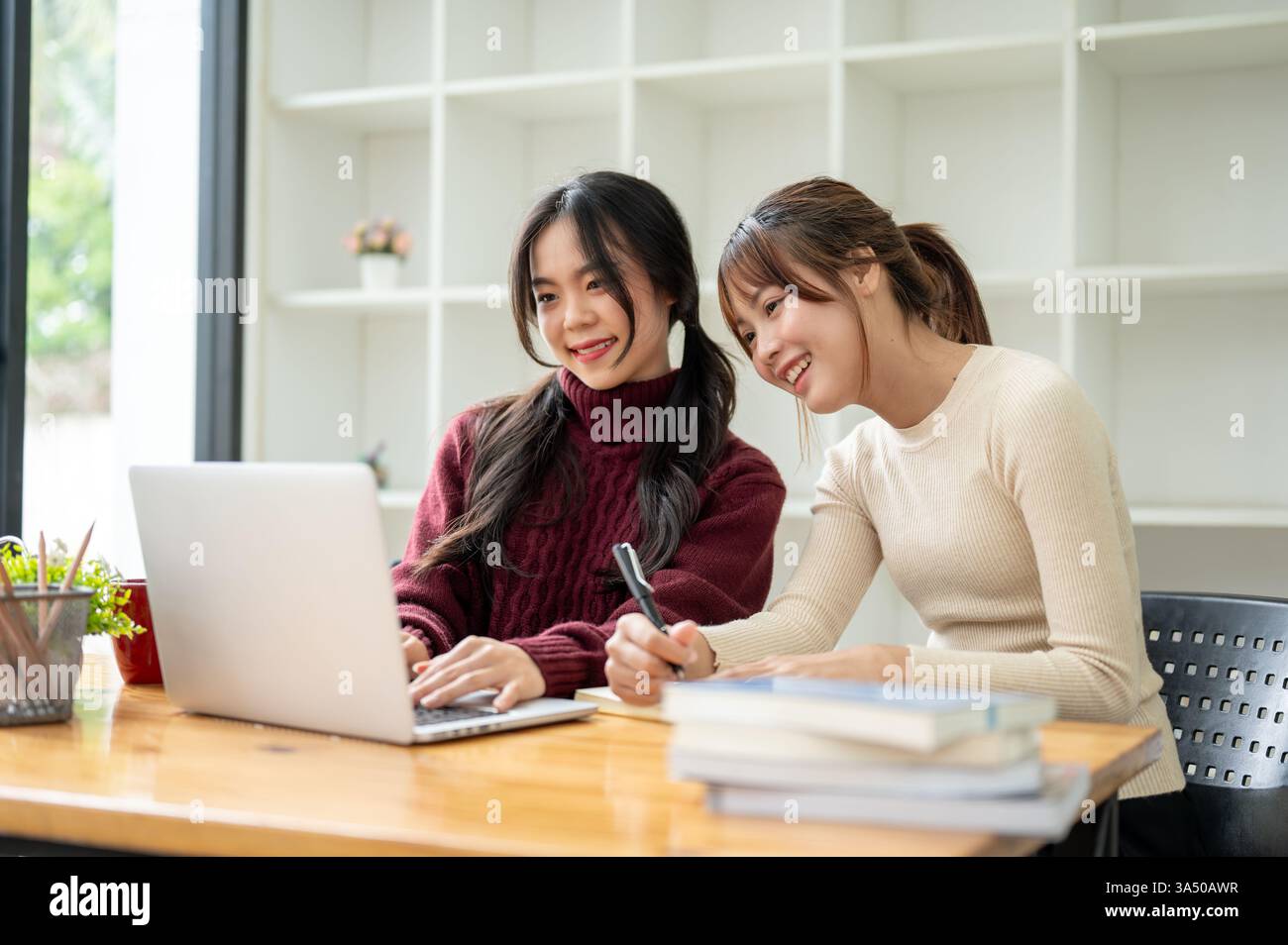 Two pretty Asian female friends are working remotely at a coffee shop ...