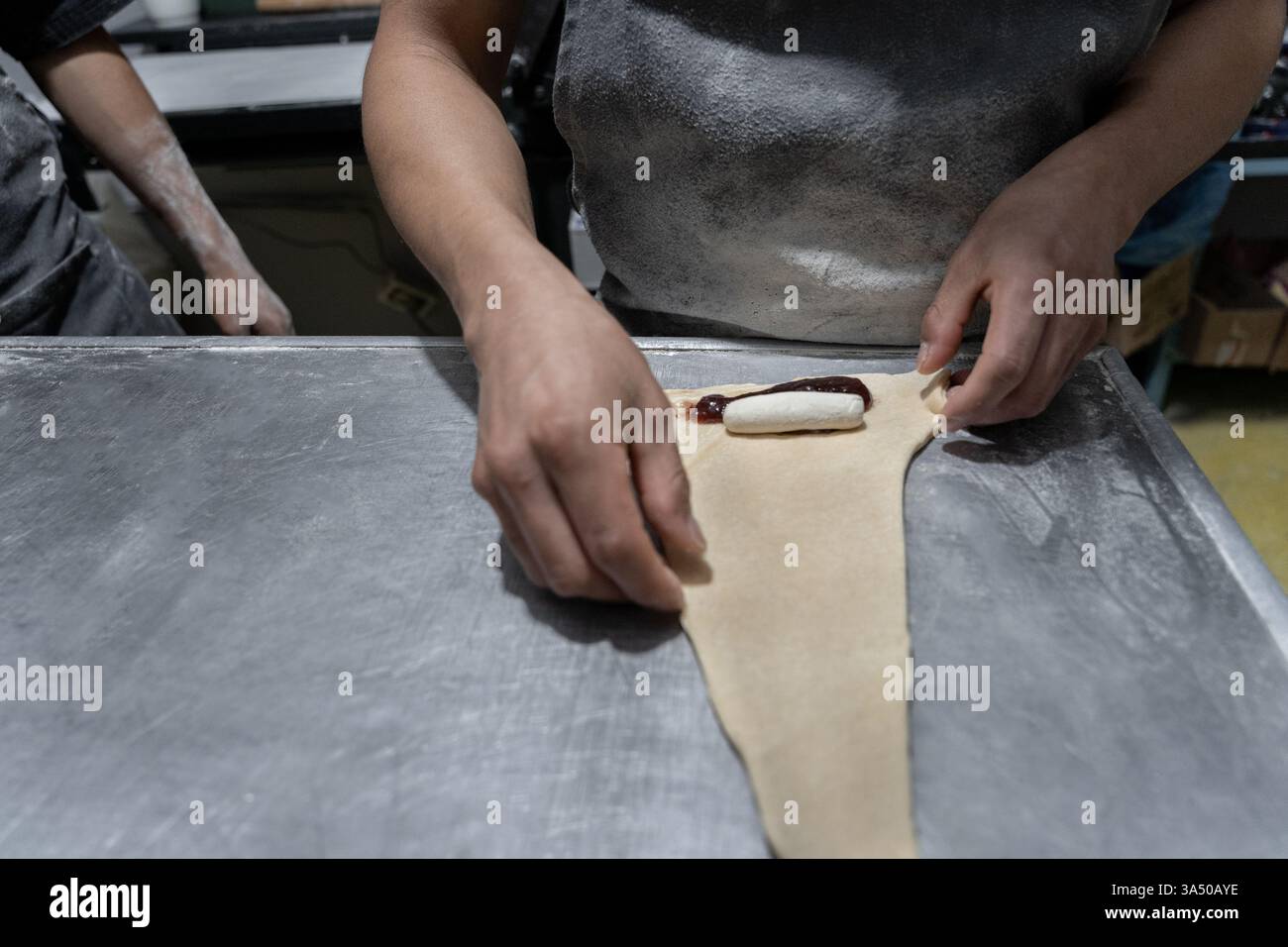 Hispanic baker is wrapping croissant triangles dough with cheese and ...