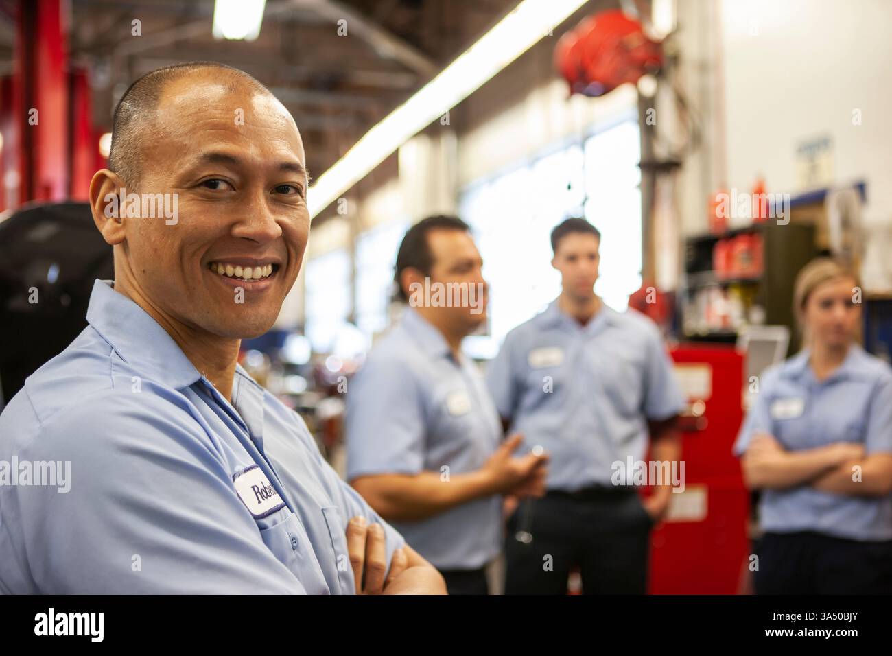 Pacific Islander man standing with team of mechanics in auto repair ...