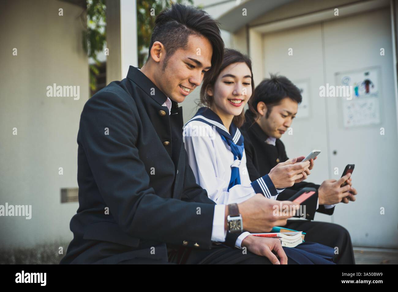 Smiling Asian male student sitting with classmates while using ...