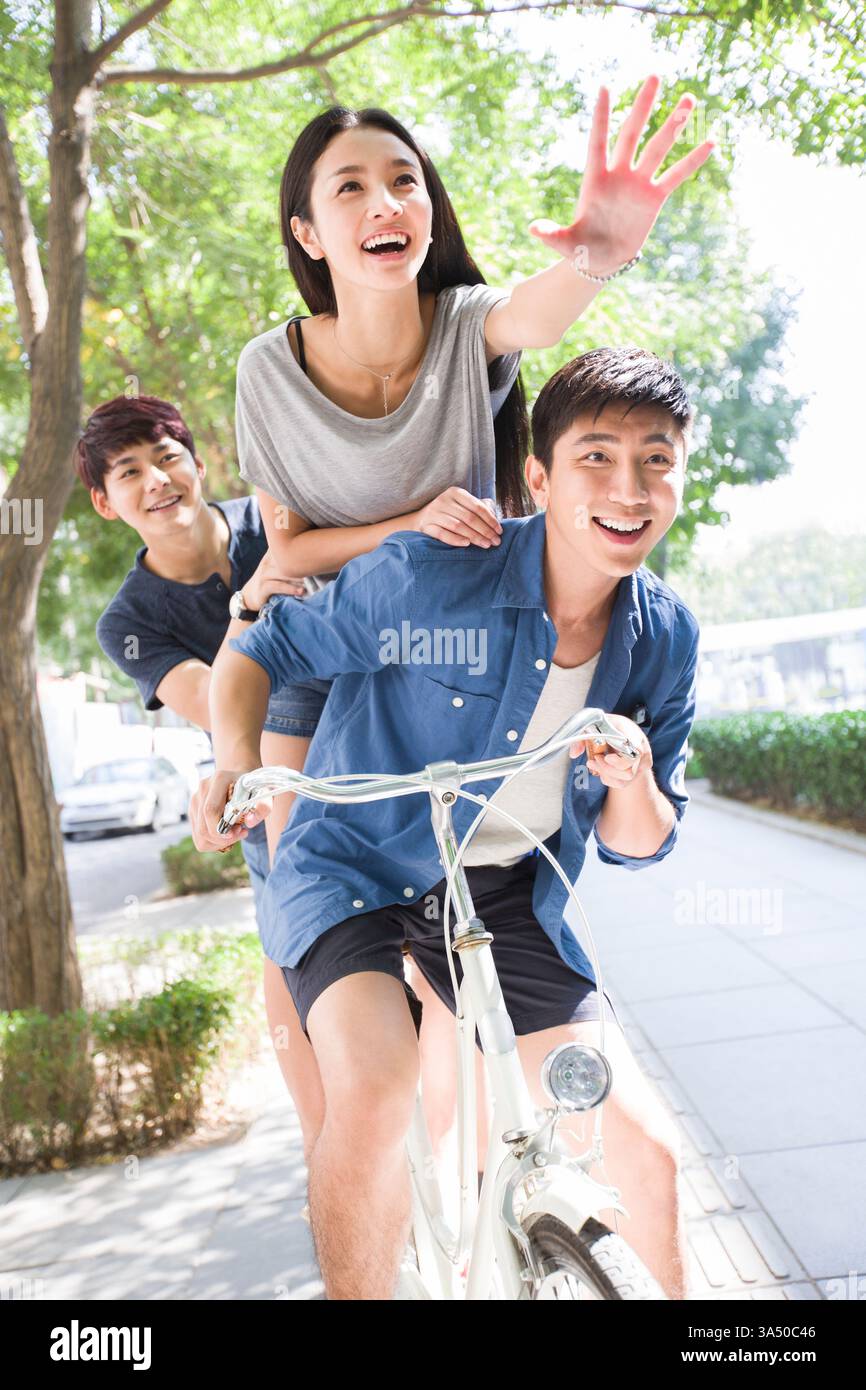 Group of young Chinese friends cycle on a university campus, capturing ...