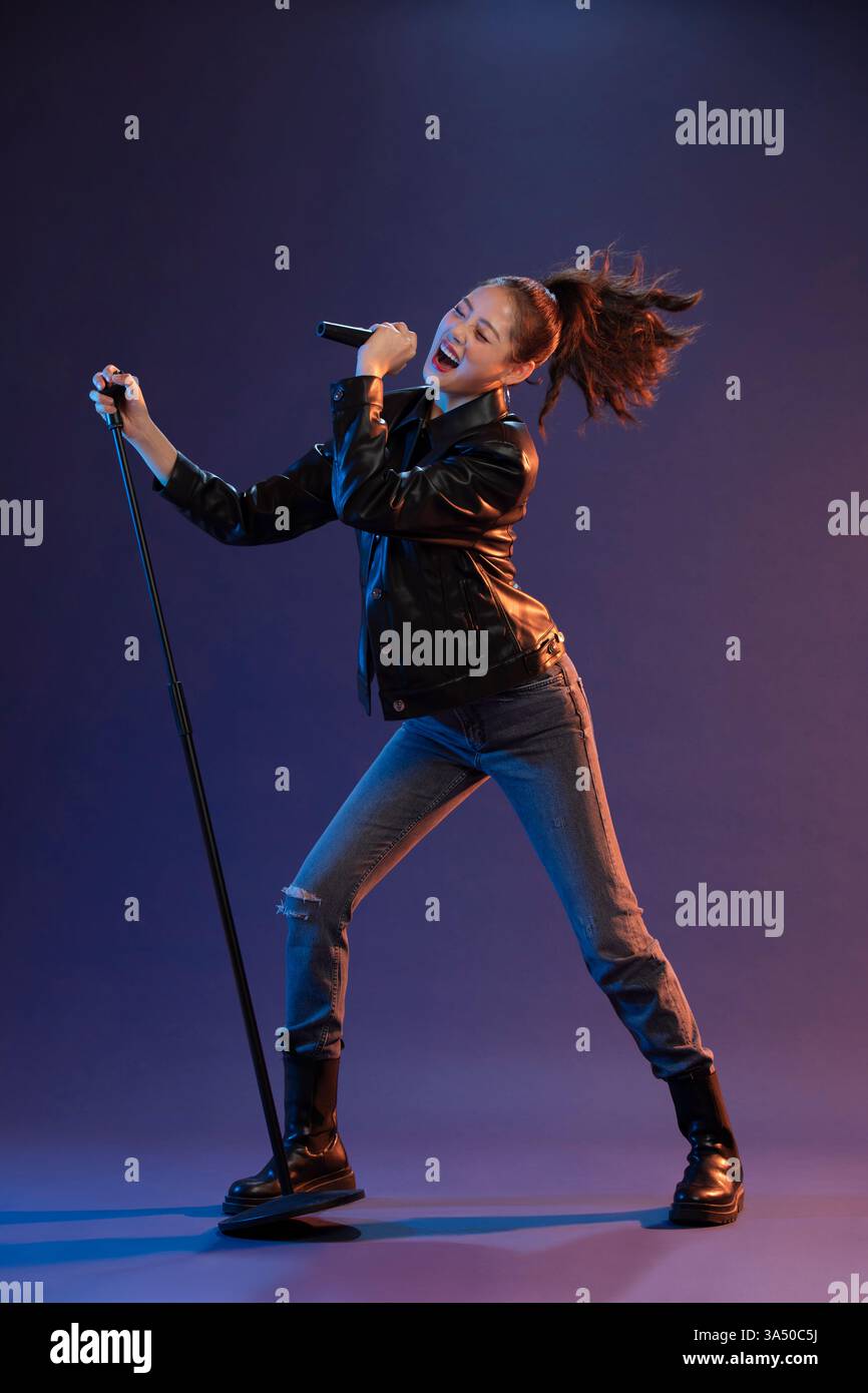Chinese woman holding microphone singing against blue background in ...