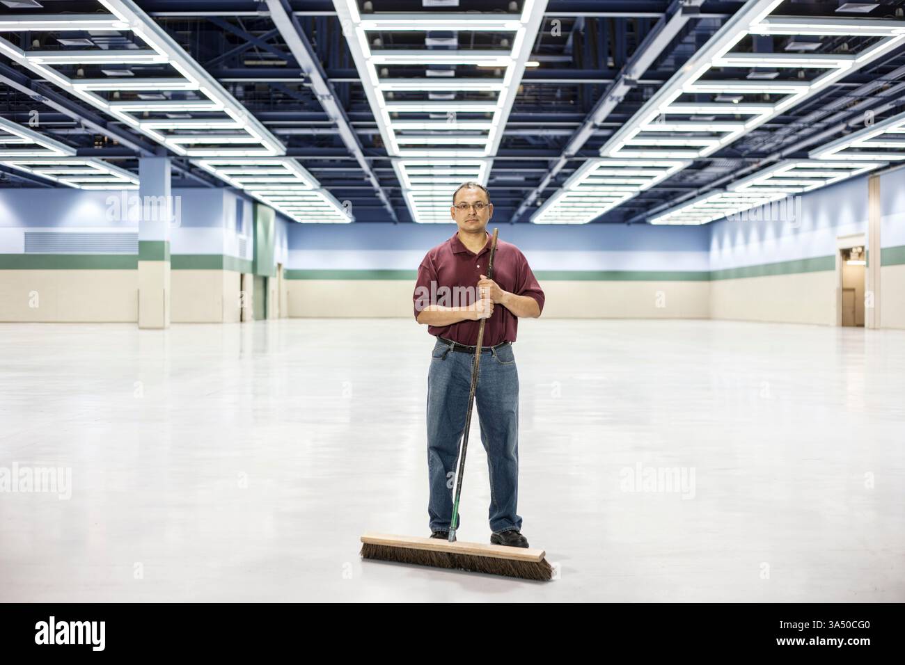 Hispanic male janitor standing with a broom in an empty convention ...