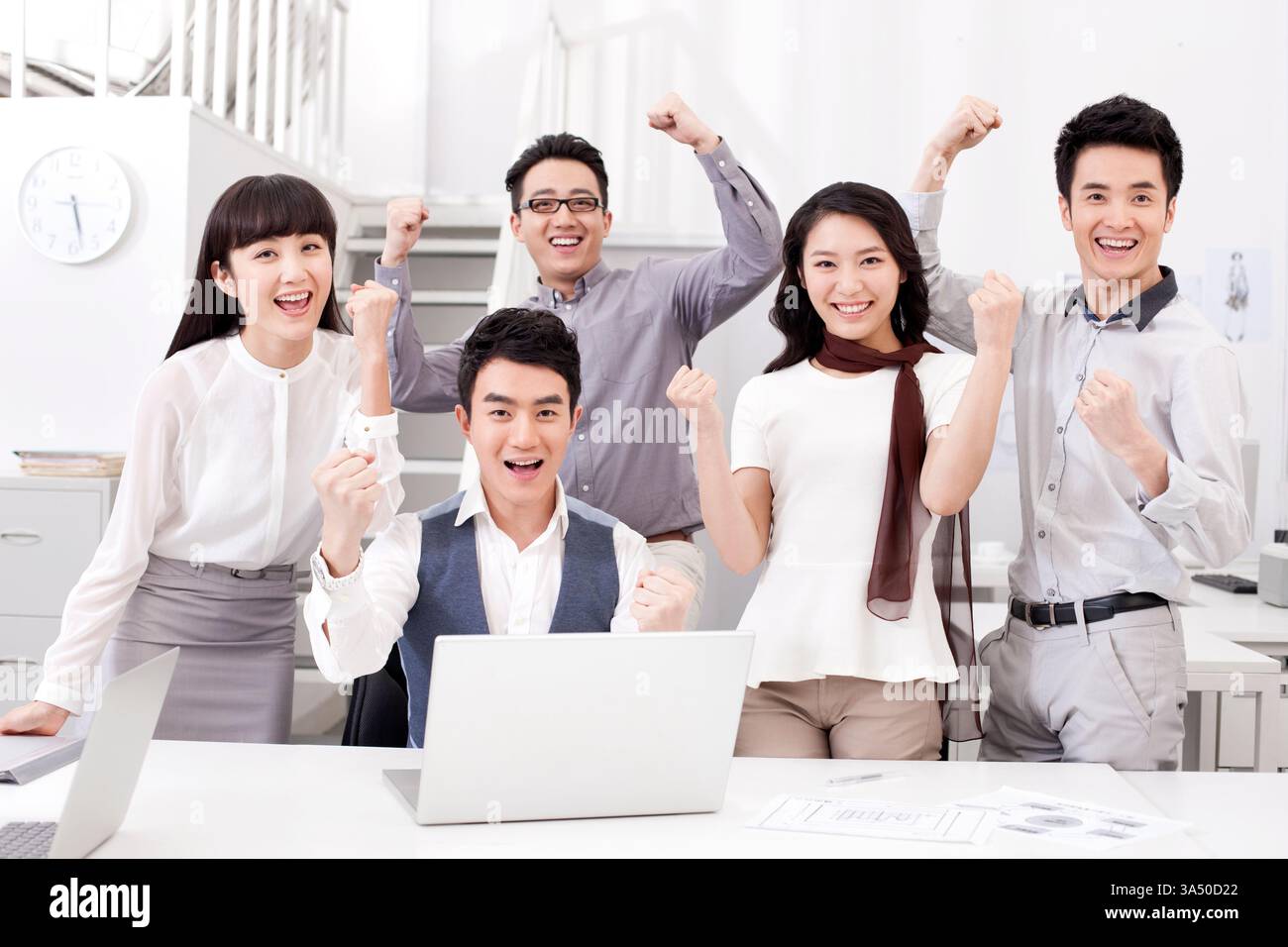 Cheerful Chinese office workers celebrate in a modern office, punching ...