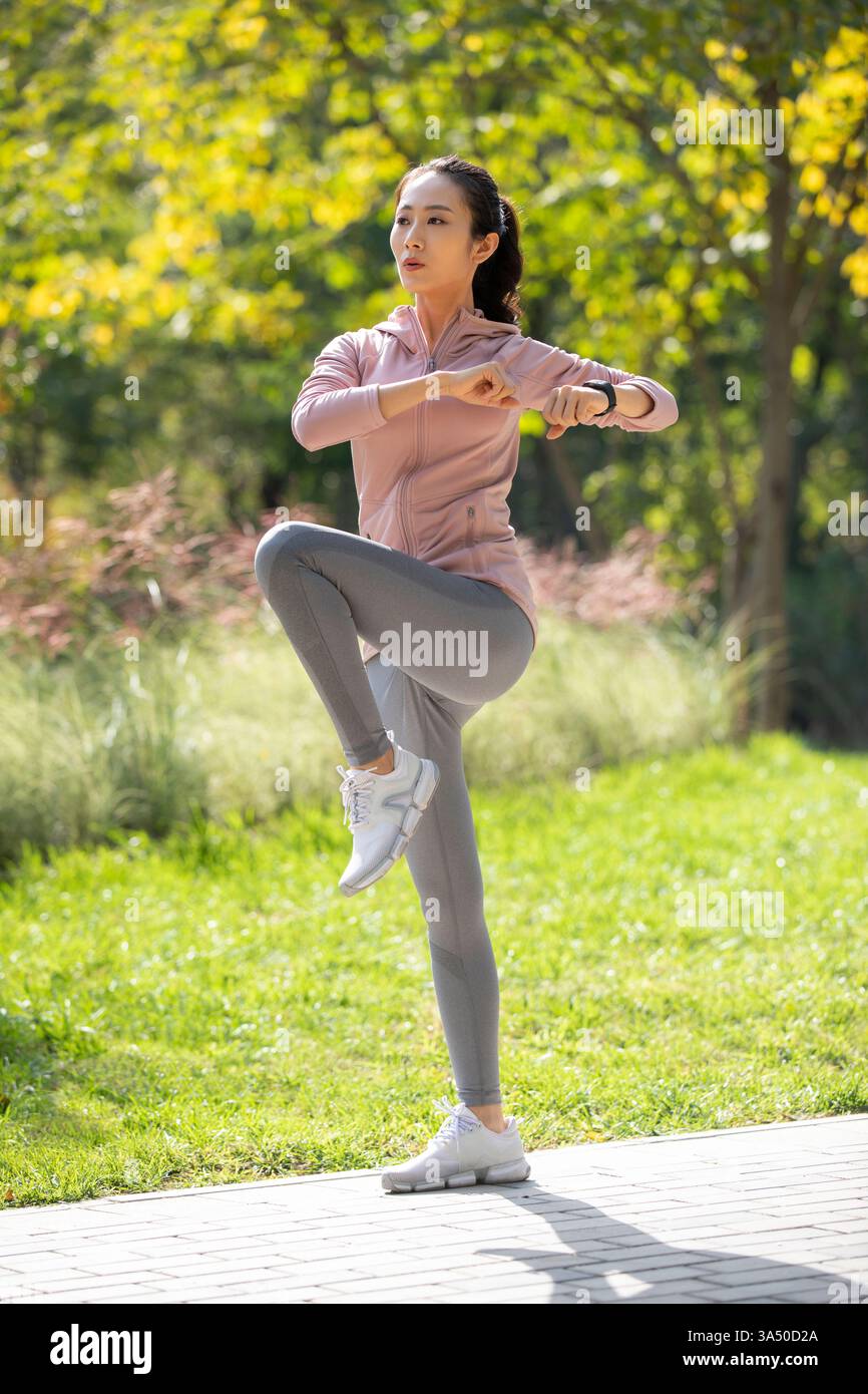 Chinese woman doing stretching exercises in park during morning workout ...