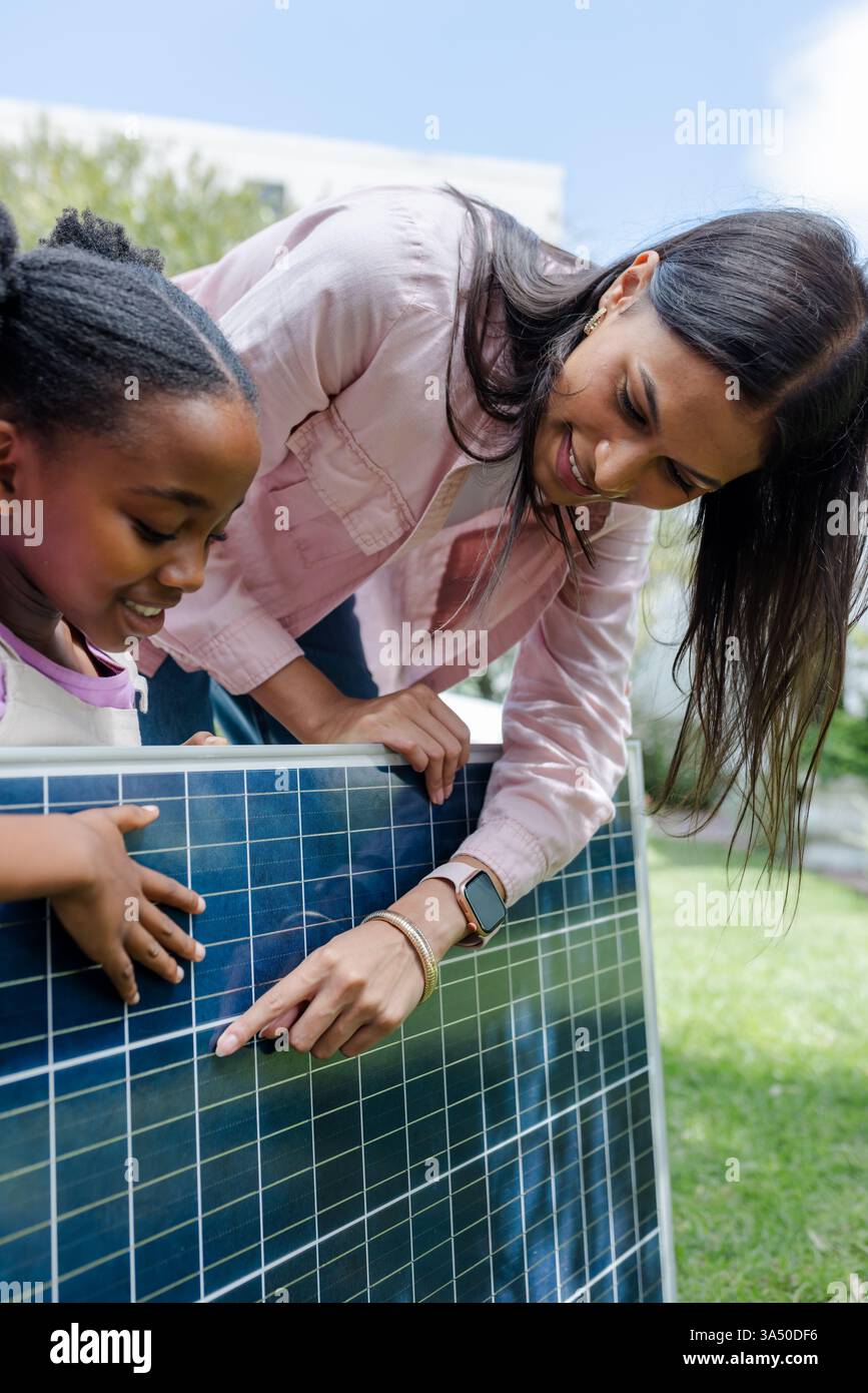 Exploring solar panel technology, mother and child learning about renewable energy outdoors ...