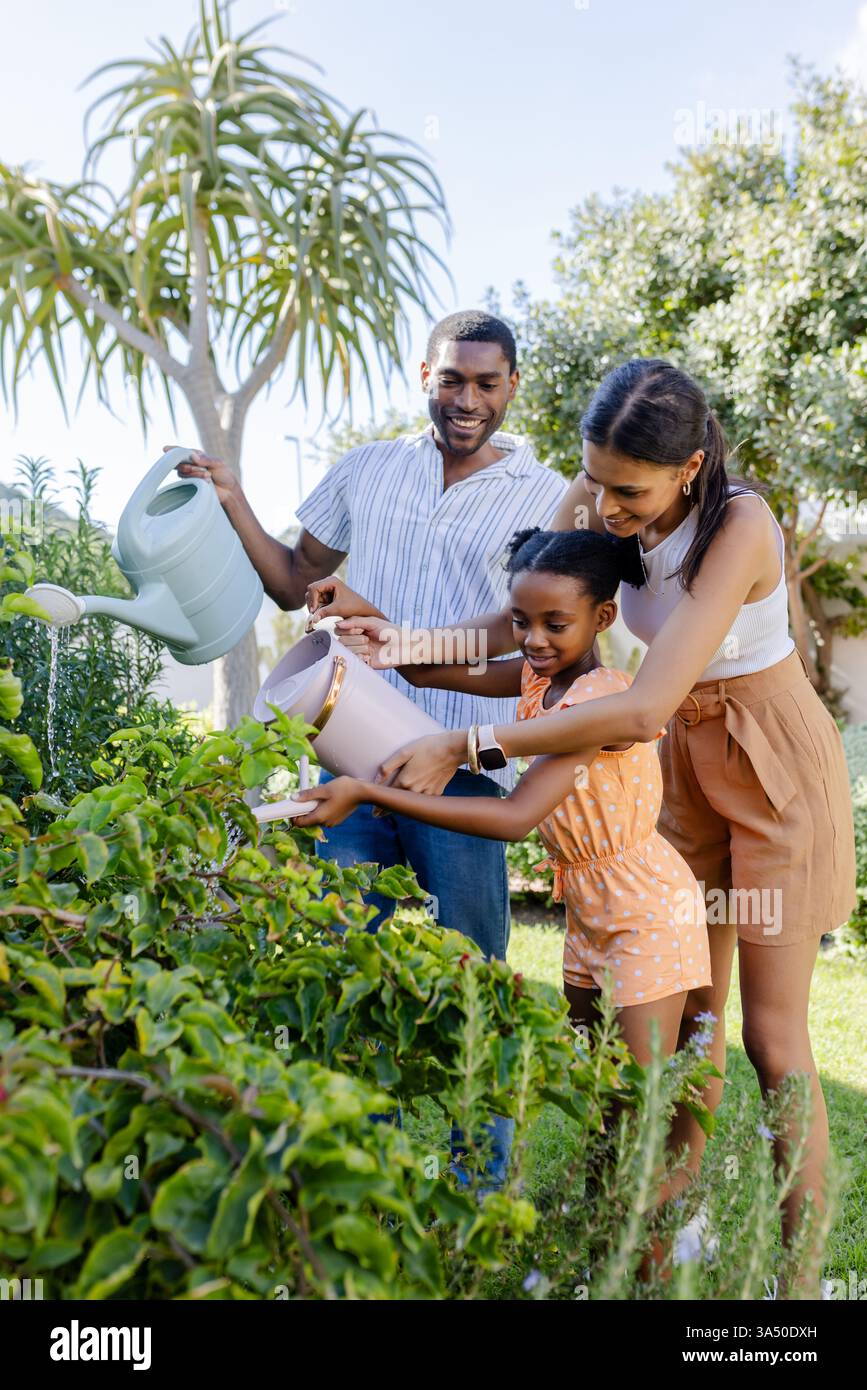 Family watering plants together in garden, enjoying quality time ...