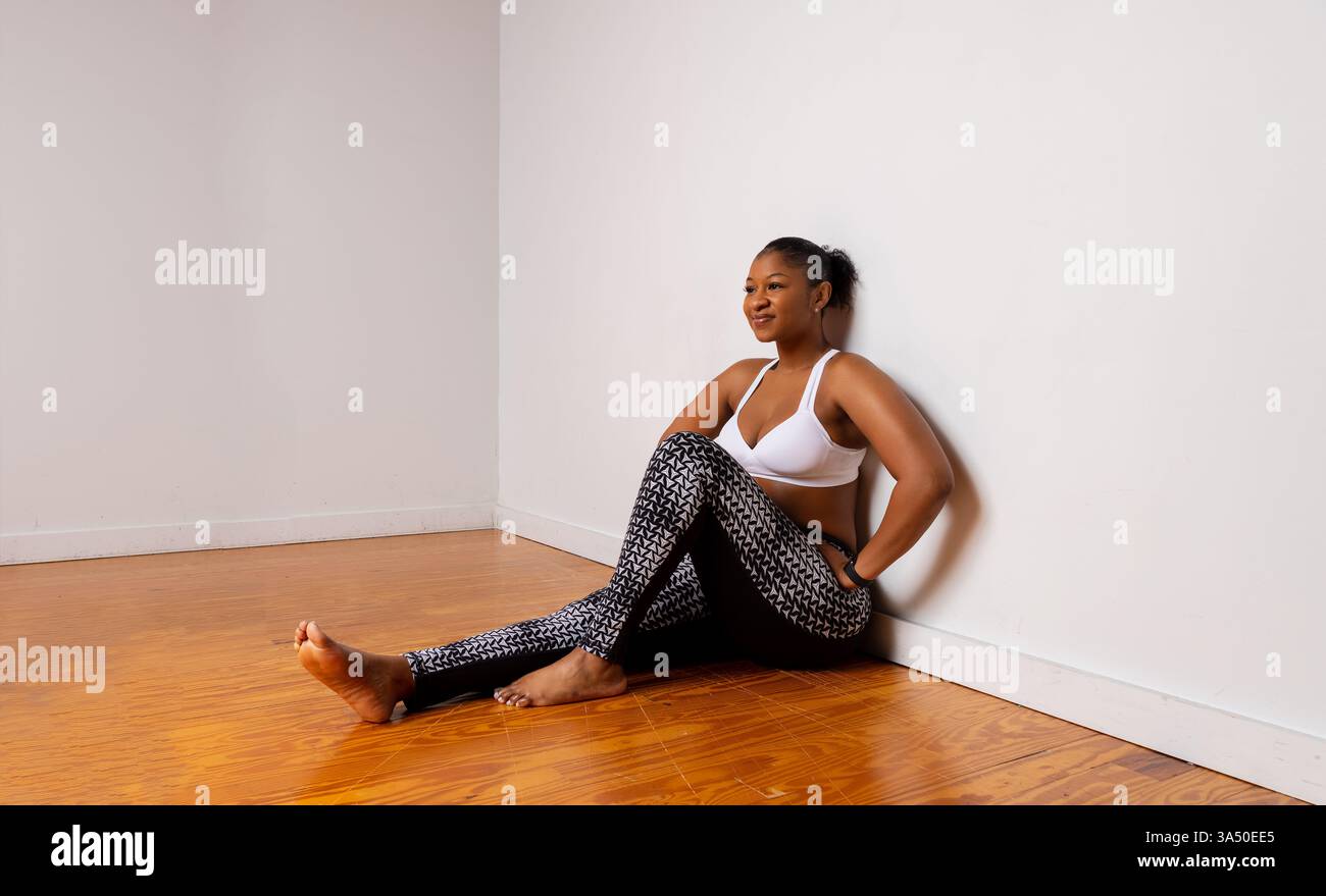 African American woman in workout clothing sitting on a hardwood floor ...