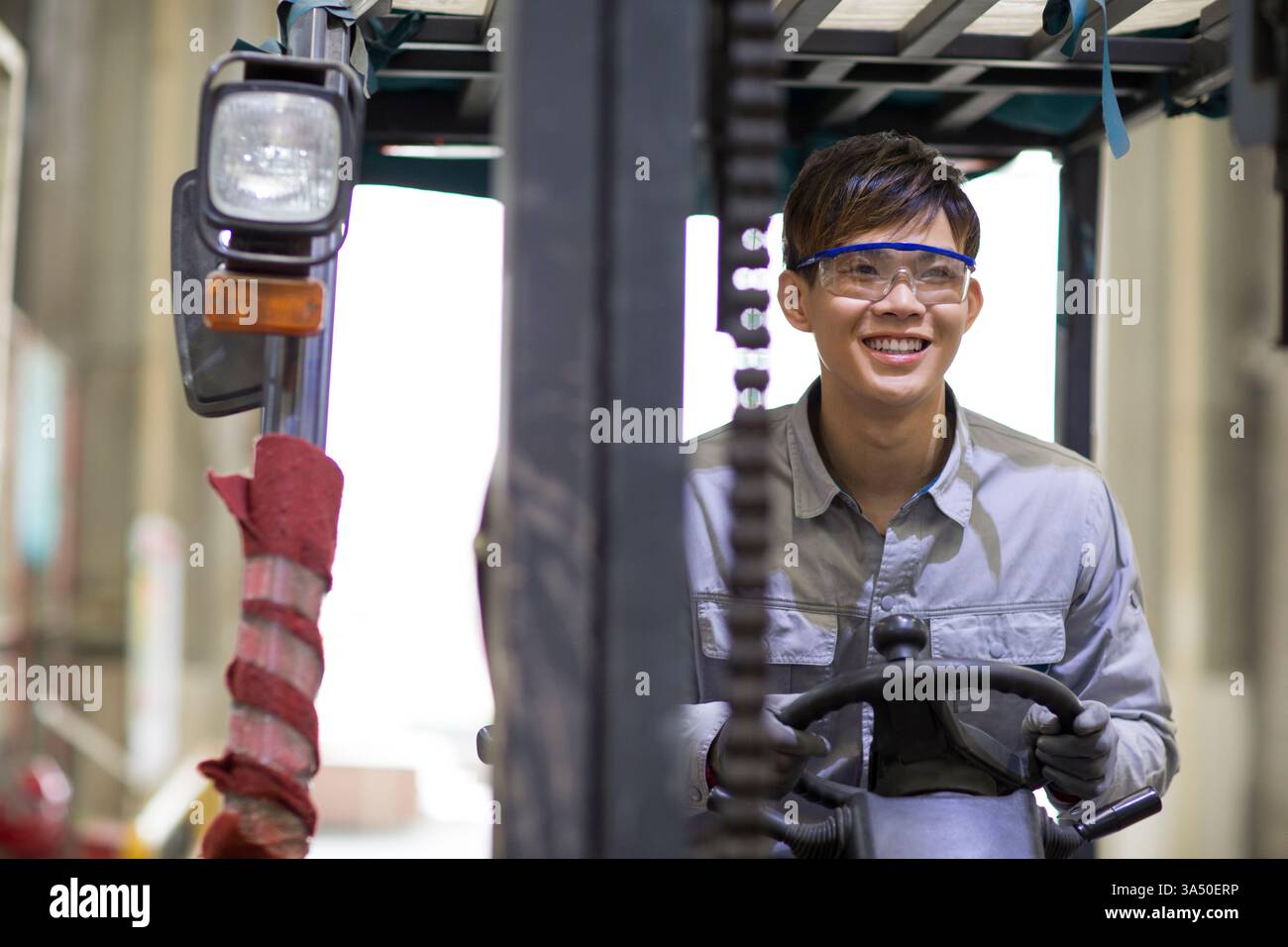 Smiling Chinese male worker in safety glasses looking away while ...