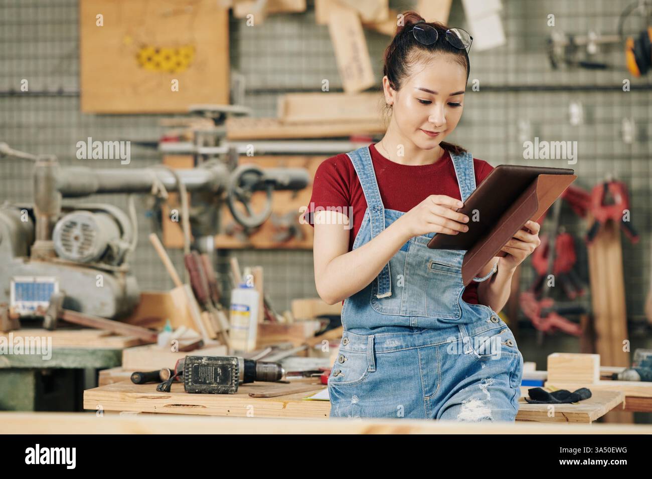 Pretty young Vietnamese carpenter in denim overall standing at ...