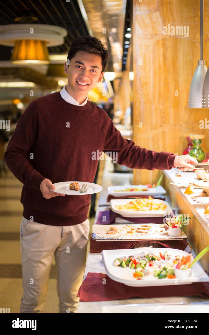 Smiling Chinese man taking food from buffet table in restaurant Stock ...