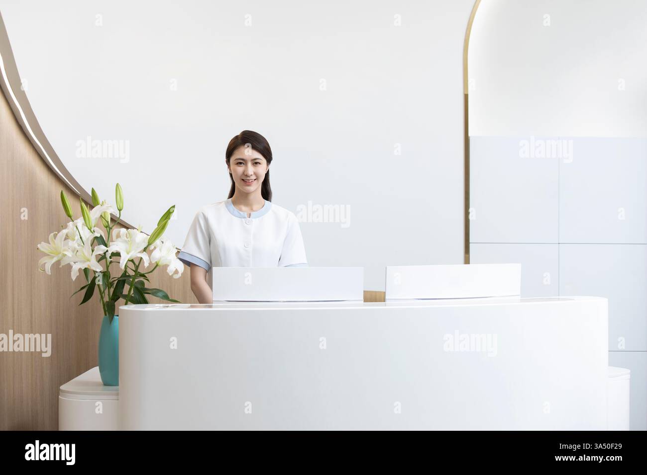 Smiling Chinese hotel receptionist standing at the front desk. This ...