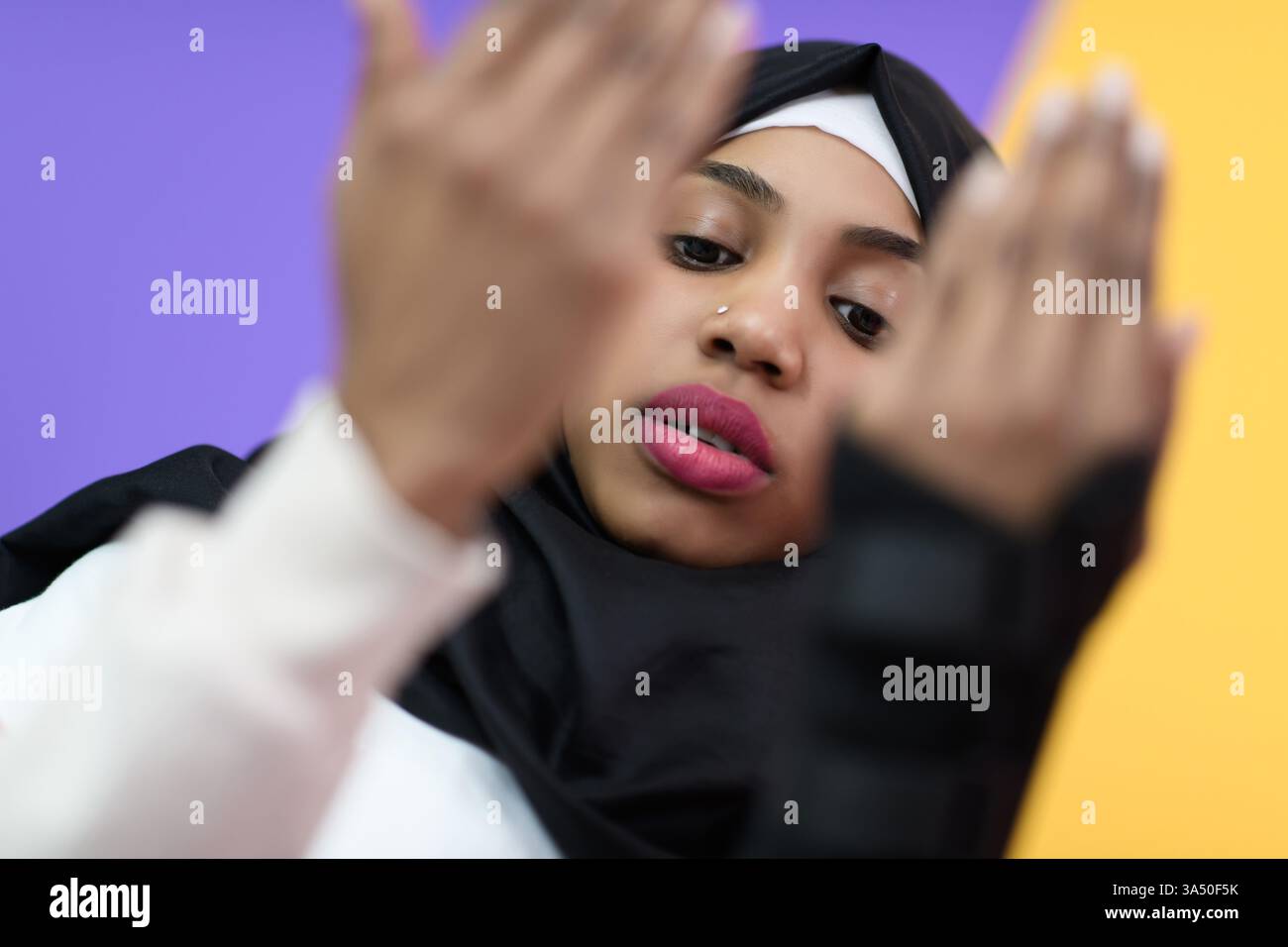 Black Muslim woman with nose piercing wearing hijab looking down while ...
