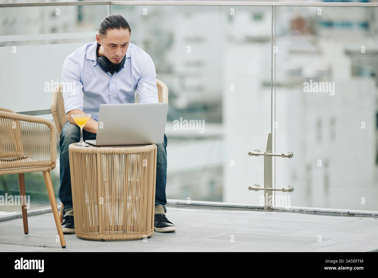 Frowning young software developer sitting on a rooftop, programming on a laptop. The scene ...