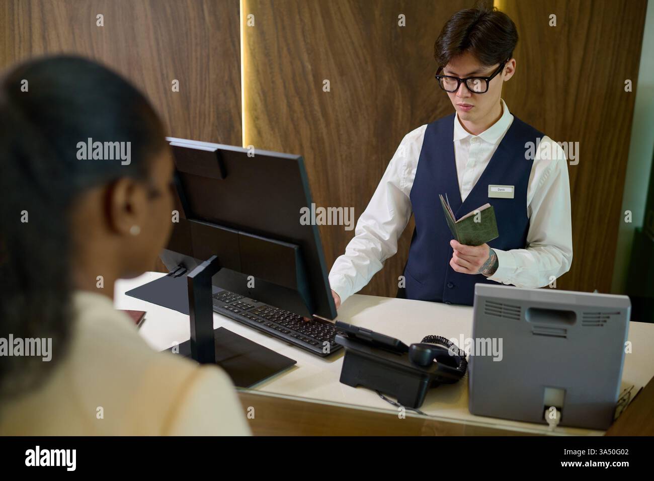 Asian male receptionist wearing eyeglasses using computer and checking ...