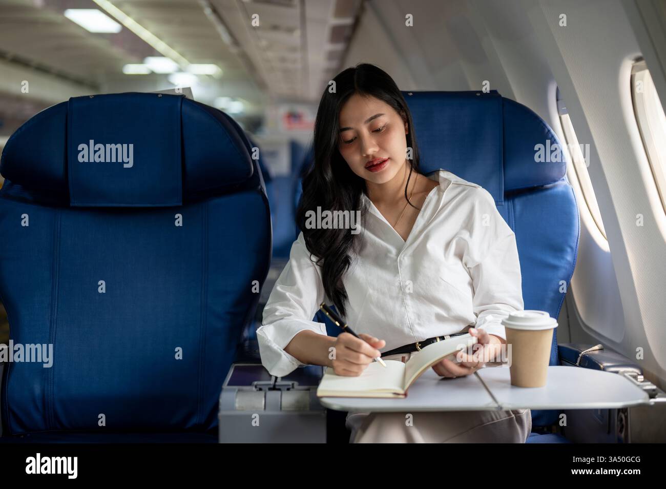 Serious Asian business woman writing in notebook sitting with crossed ...