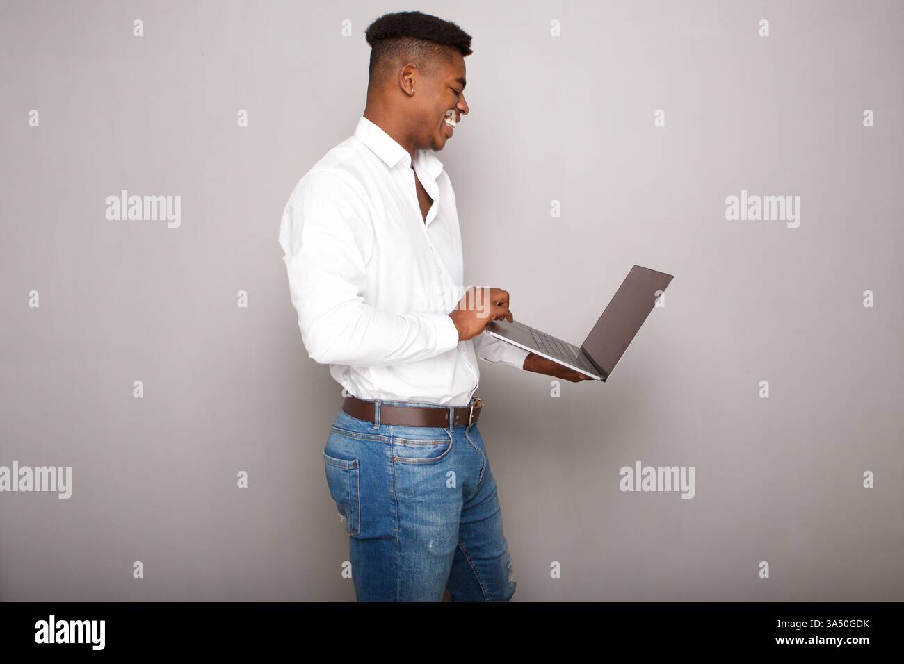 Smiling Black man with laptop standing against gray wall Stock Photo ...