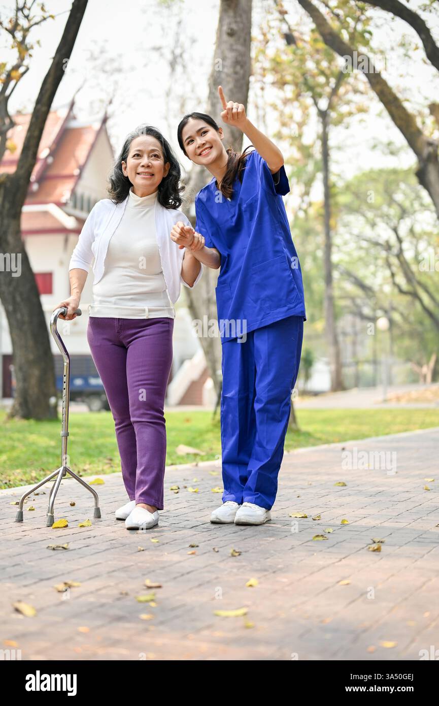 Smiling Asian female caregiver in blue uniform pointing finger away ...