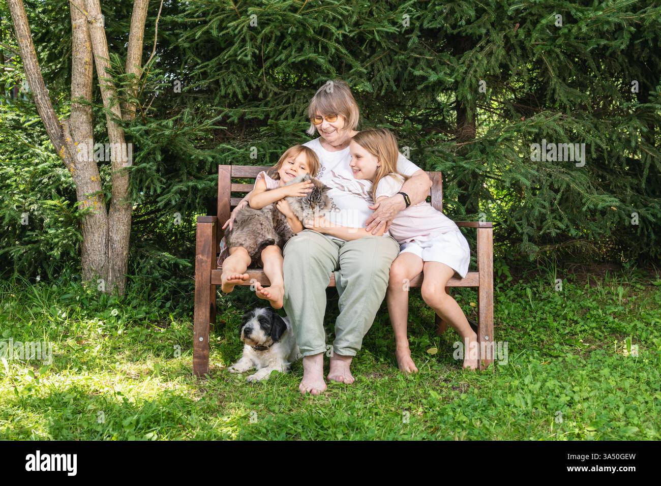 A grandmother sits on a wooden bench in a summer garden, hugging her ...