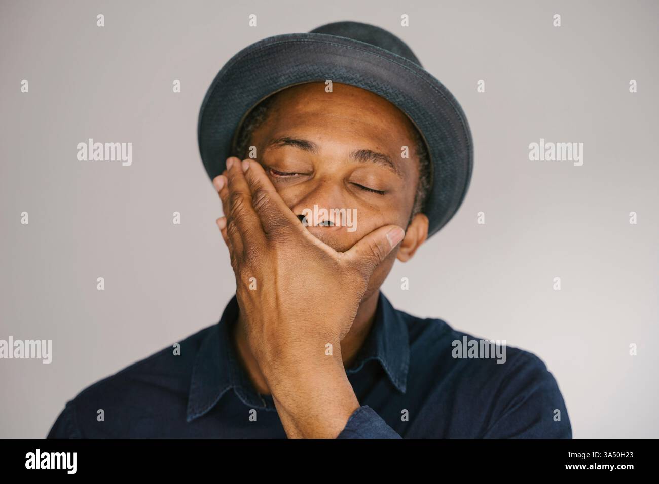 Black male with anguished expression covering mouth with hands standing ...