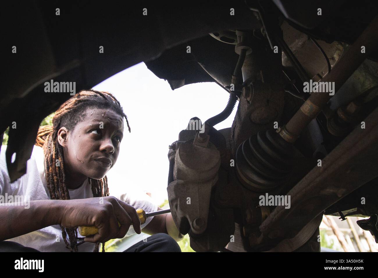 Black female mechanic crouching fixing broken car on street on sunny ...