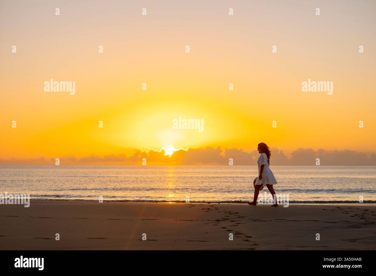 A woman enjoys a calm walk along a sandy beach as the sun rises ...