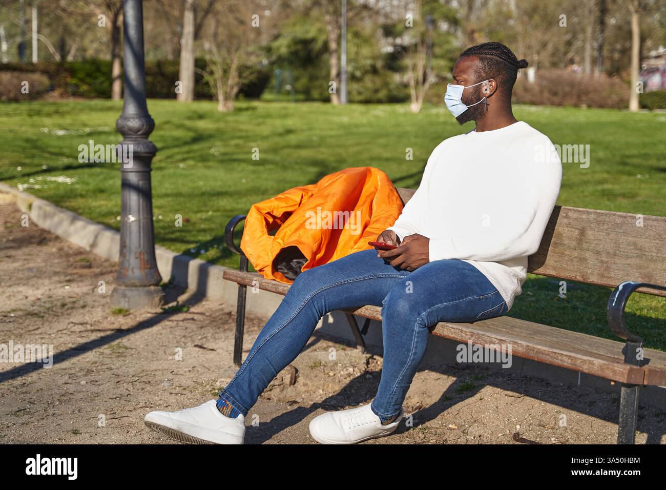 Black man in mask sitting on bench looking away outdoors Stock Photo ...
