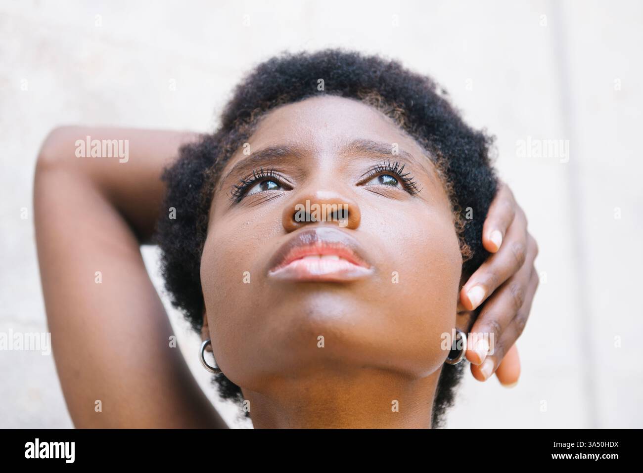 Black woman looking up standing with hand over head against wall Stock ...