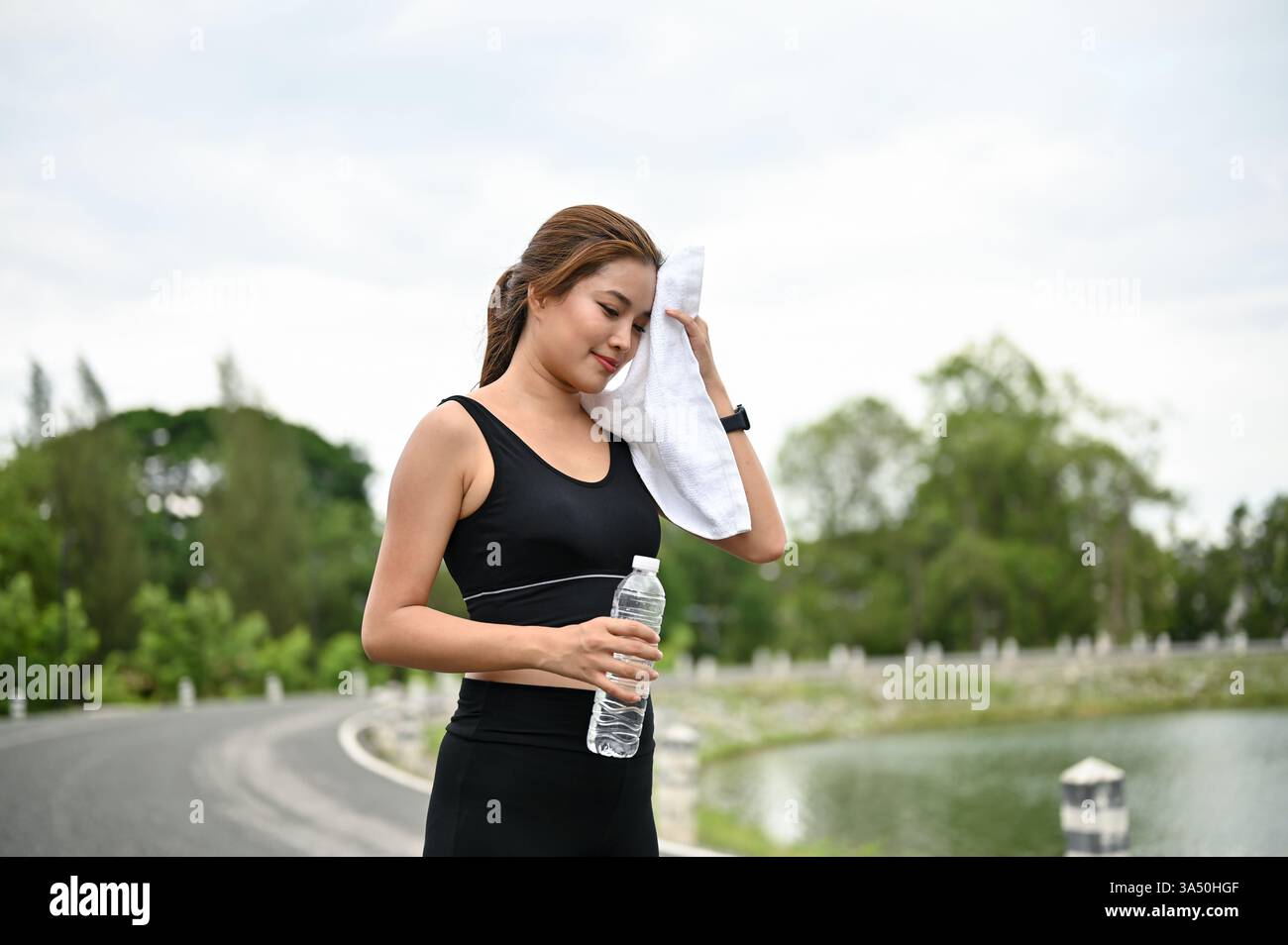 A tired and sweaty Asian woman in sportswear is walking slowly, wiping her sweat with a towel ...