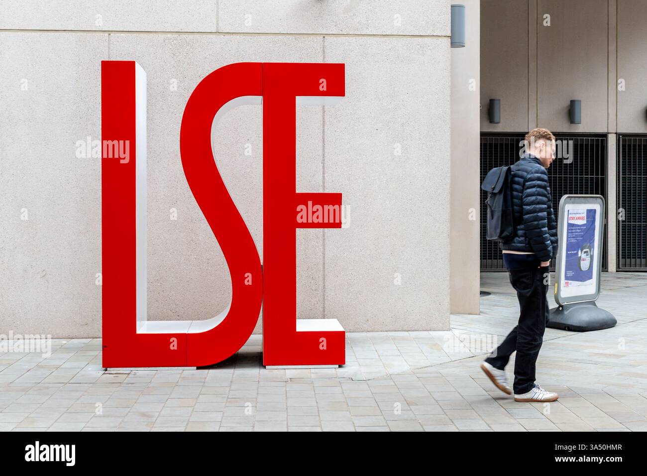 LSE large red letters at London School of Economics and Political Science with young man walking ...