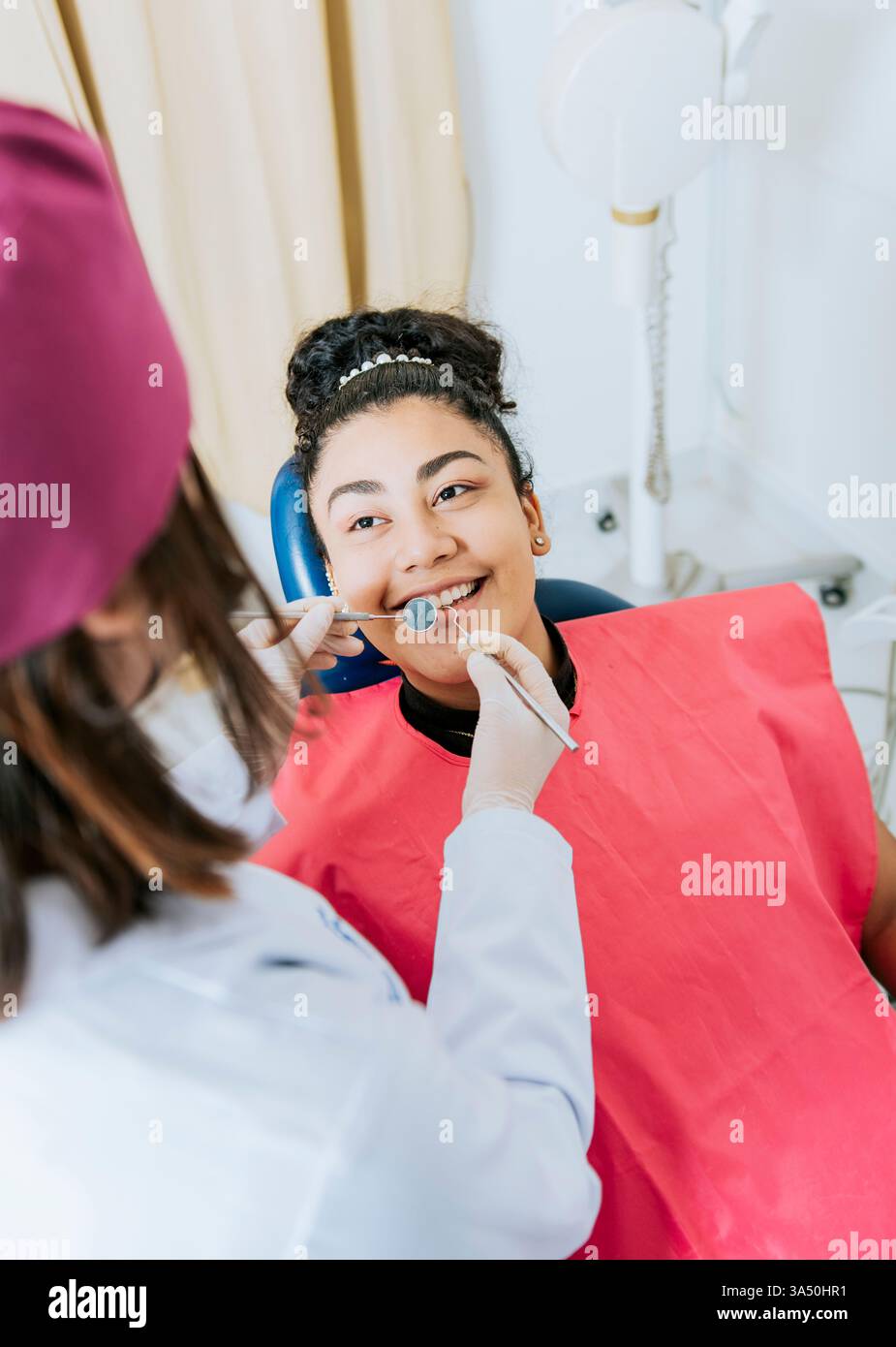 Smiling Hispanic female patient lying on dental chair with Hispanic female dentist standing ...