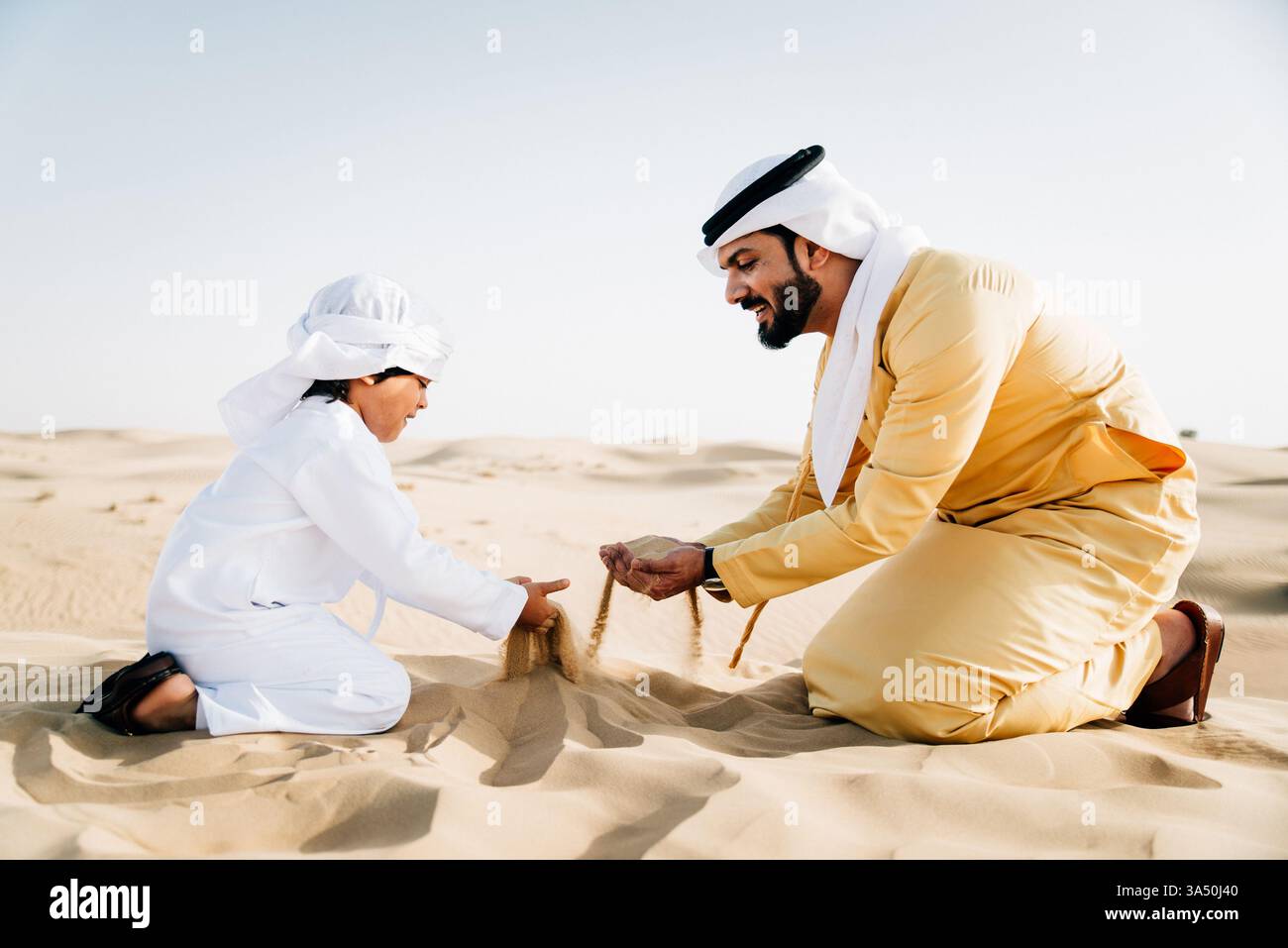 Cheerful Middle Eastern father kneeling and playing sand with son on ...